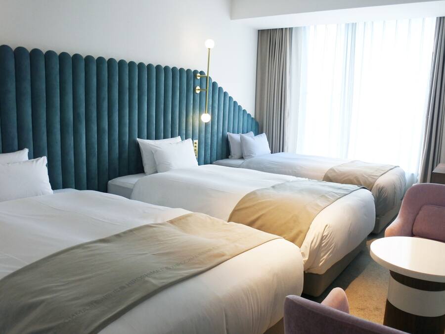 Quarto de hotel com três camas, uma mesa pequena e uma cadeira.