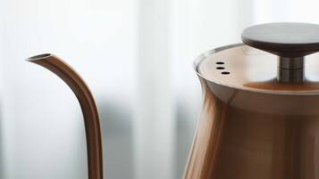 Uma cafeteira de cor cobre com bico e tampa sobre uma superfície branca.