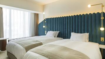 Quarto de hotel com duas camas, uma mesa redonda e uma janela grande com cortinas.