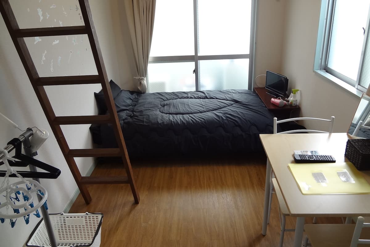 Quarto com cama, escrivaninha, cadeira, escada, janela com cortinas e luminária pendente.