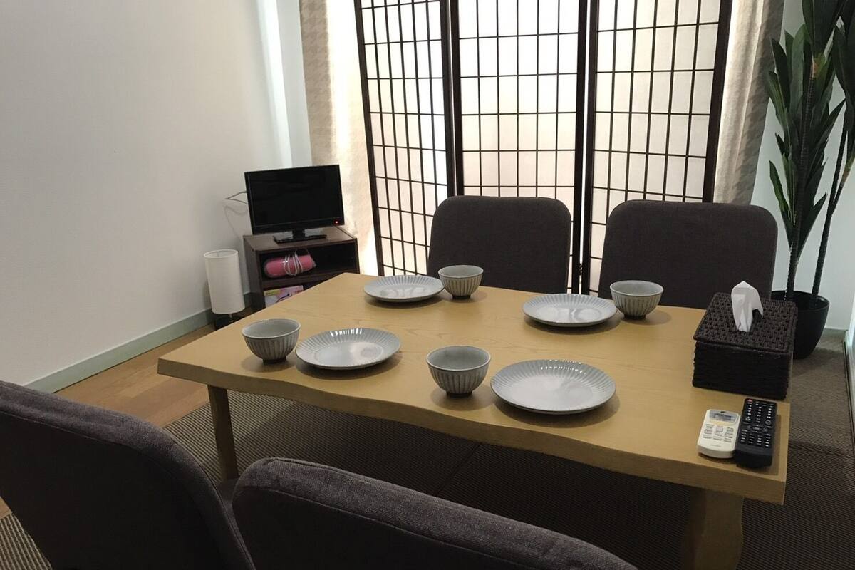 Uma mesa de jantar posta com pratos, tigelas e uma caixa de lenços, com cadeiras ao redor.