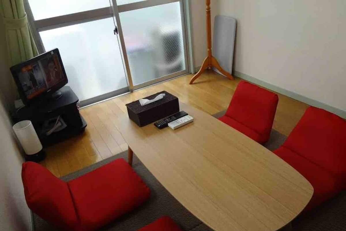 Uma sala de estar moderna com uma mesa de madeira, assentos acolchoados vermelhos, uma televisão e um alto-falante.
