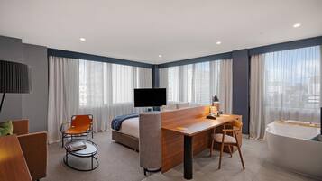Quarto de hotel moderno com cama, escrivaninha, cadeira e banheira.
