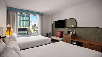 Quarto de hotel com duas camas, uma escrivaninha, televisão e janela com vista para edifícios.