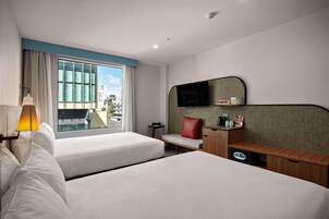 Quarto de hotel com duas camas, uma escrivaninha, televisão e janela com vista para edifícios.