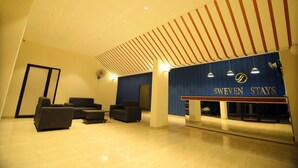 Um hall de entrada com balcão de recepção, sofás e uma parede azul com o nome 'SWEVEN STAYS'.