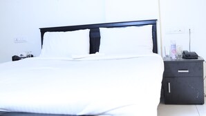 Quarto de hotel com cama, mesa de cabeceira, telefone e um pequeno armário.