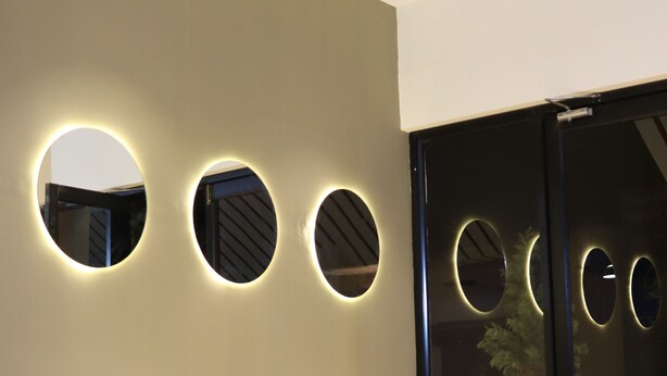 Interior moderno com luminárias circulares na parede e uma porta de vidro.