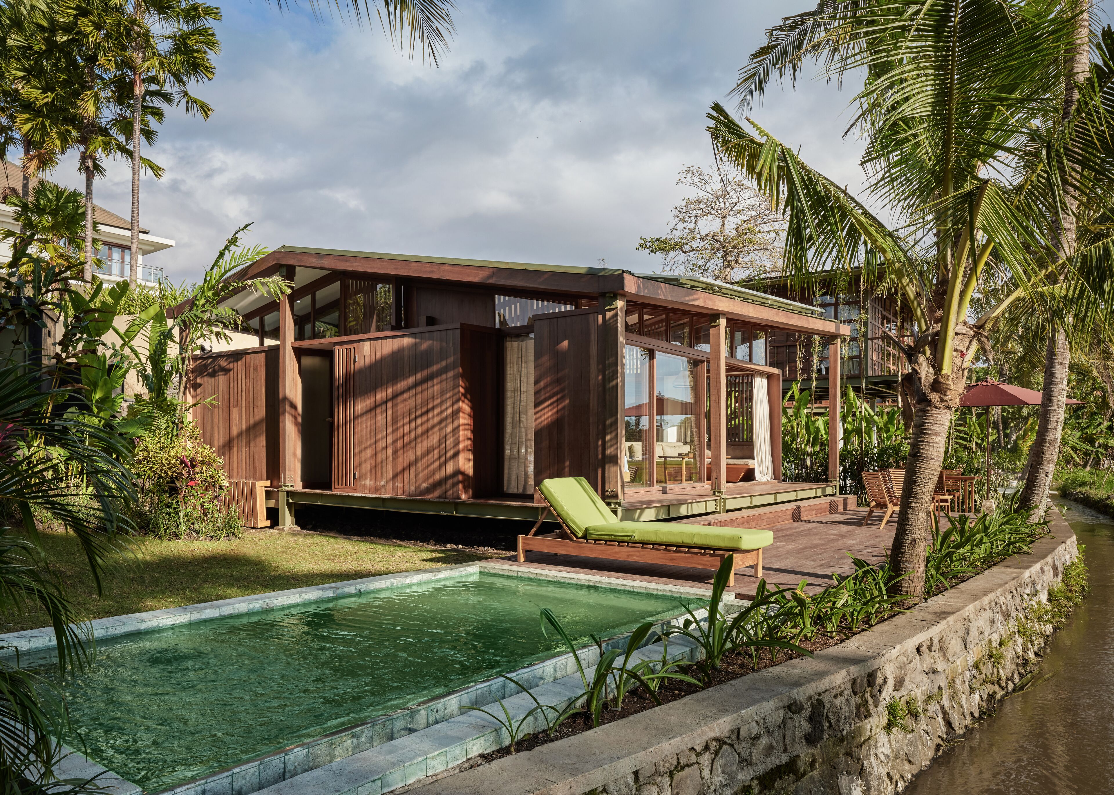 Uma villa de madeira com piscina, rodeada por vegetação exuberante e palmeiras.