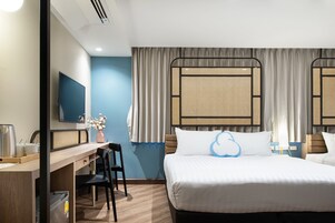 Quarto de hotel com cama, secretária com cadeira, televisão e janela com cortinas.