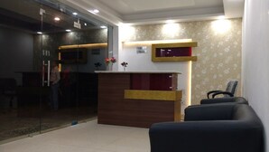 Uma área de recepção com balcão de madeira, divisória de vidro e sala de espera com cadeiras.