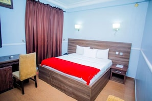 Quarto de hotel com uma cama de madeira, uma escrivaninha e uma cadeira.