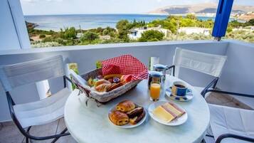 Uma varanda com uma mesa posta para o café da manhã, incluindo croissants, uma cesta de frutas e um copo de suco de laranja.