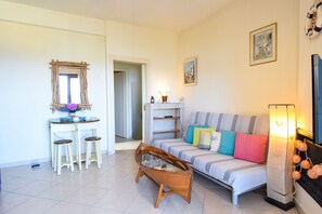 Uma sala de estar com sofá, uma mesa pequena com banquetas, mesa de centro de madeira, luminária e um quadro na parede.