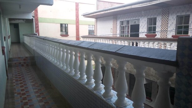 Um corredor com piso ladrilhado, balaustrada branca e um edifício com janelas estampadas e a placa com o número 28.