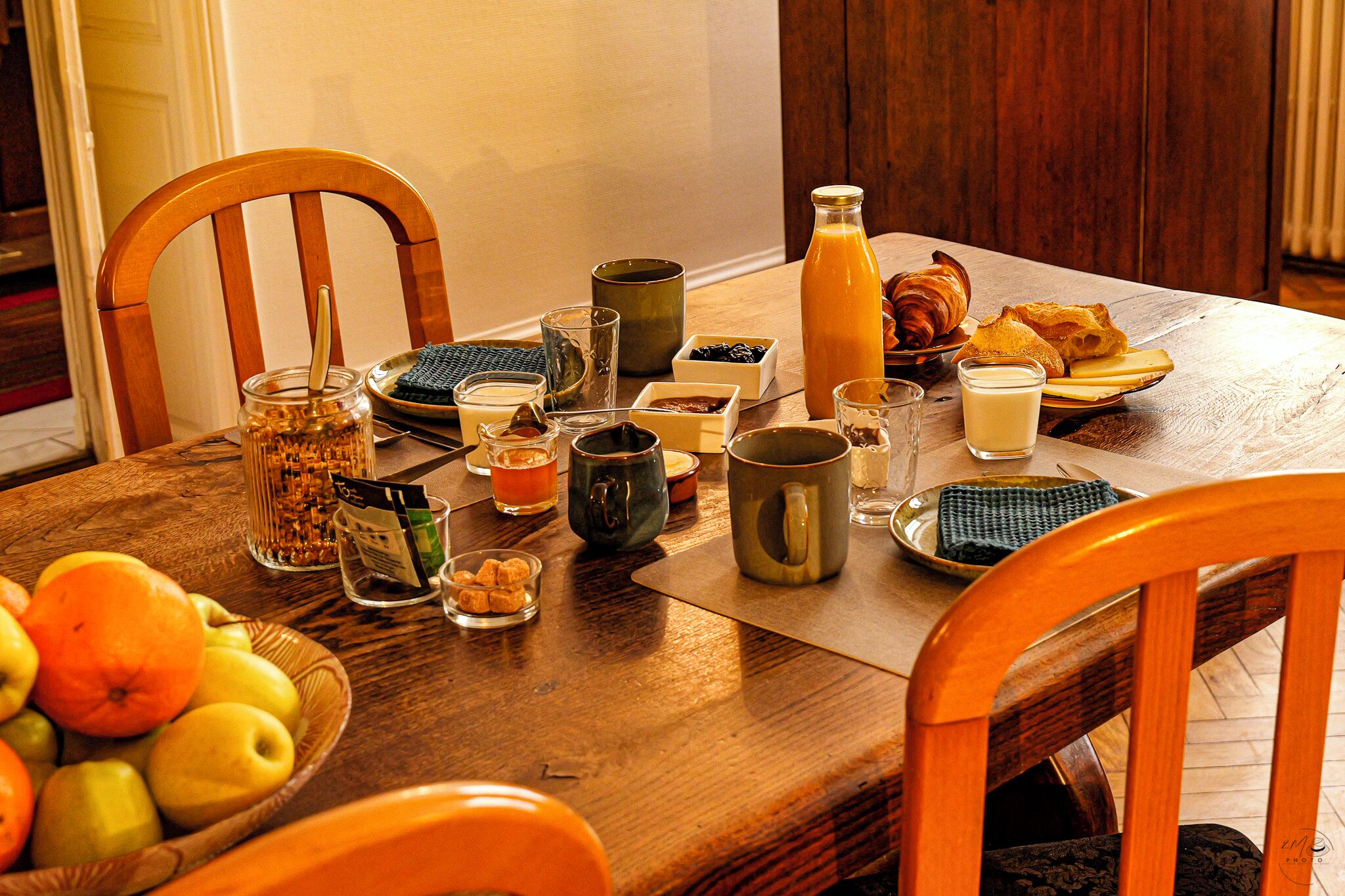 Uma mesa de café da manhã com diversos alimentos, bebidas e uma cesta de frutas.