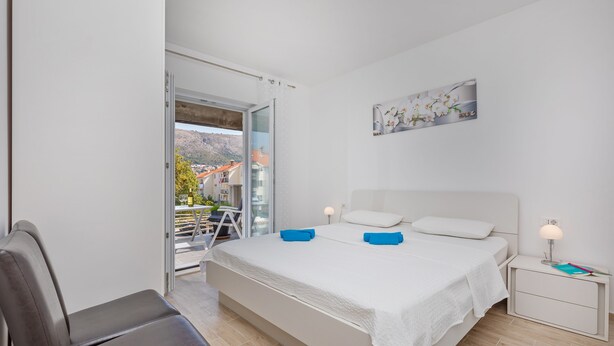 Quarto com cama, poltrona, mesa de cabeceira, abajur e um quadro na parede.