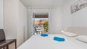 Quarto de hotel com cama, uma cadeira, um quadro e vista para edifícios e uma palmeira.
