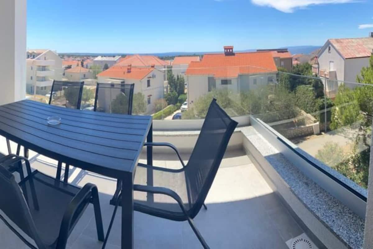 Uma varanda com mesa e cadeiras, com vista para uma área residencial com casas de telhado vermelho.