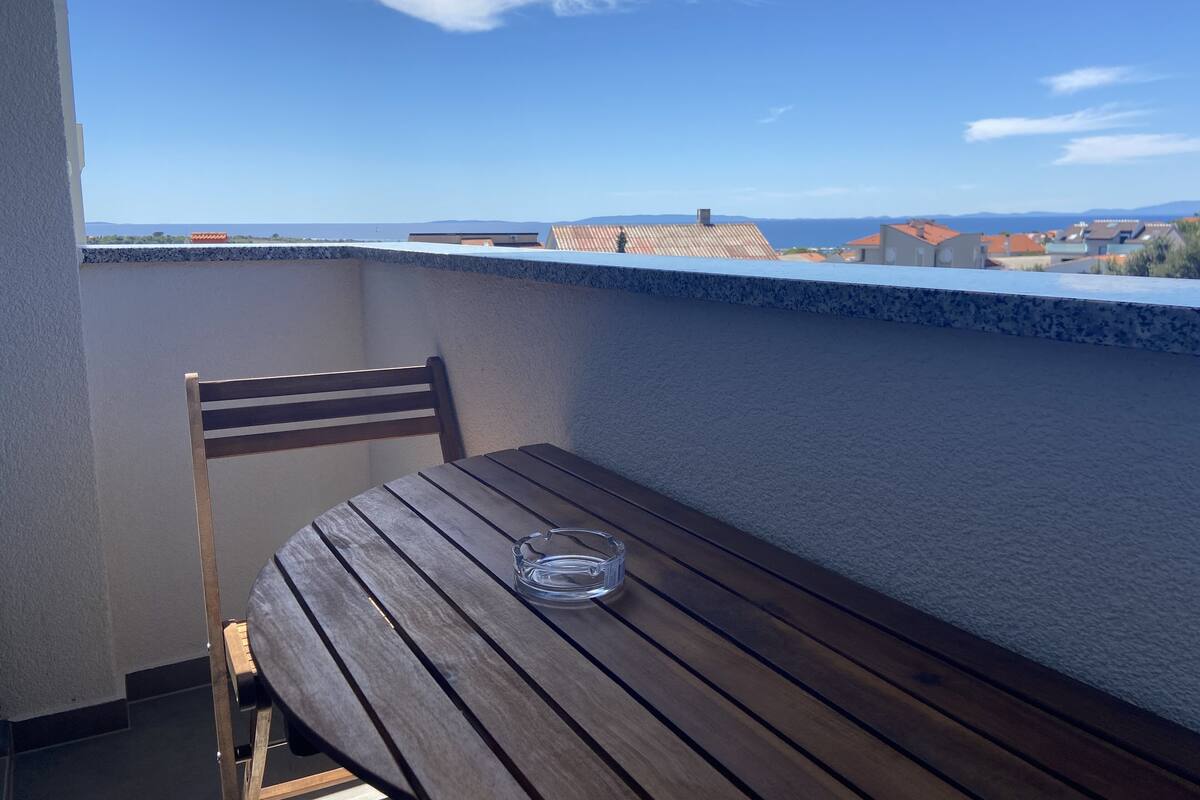 Uma mesa de madeira com um copo, uma cadeira e vista para edifícios e montanhas ao fundo.