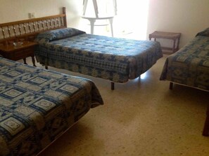 Quarto com três camas, cada uma com colcha estampada, cabeceira de madeira e mesa de cabeceira pequena de madeira.