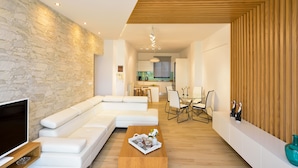 Uma sala de estar moderna com parede de pedra, sofá branco, mesa de centro de madeira e uma área de jantar com cadeiras e mesa.