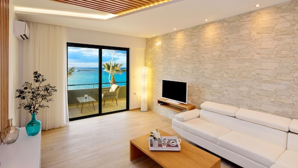 Uma sala de estar moderna com um sofá branco, uma mesa de centro de madeira e uma TV em uma parede de pedra.