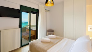 Quarto de hotel com uma cama, uma cadeira, televisão fixada na parede e vista para o mar por uma porta deslizante.