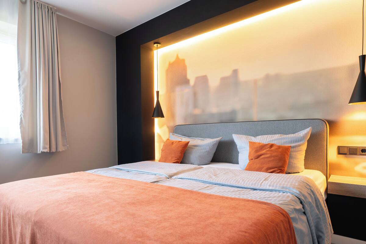 Quarto de hotel moderno com uma cama grande, arte com tema urbano na parede e vista para o horizonte da cidade.