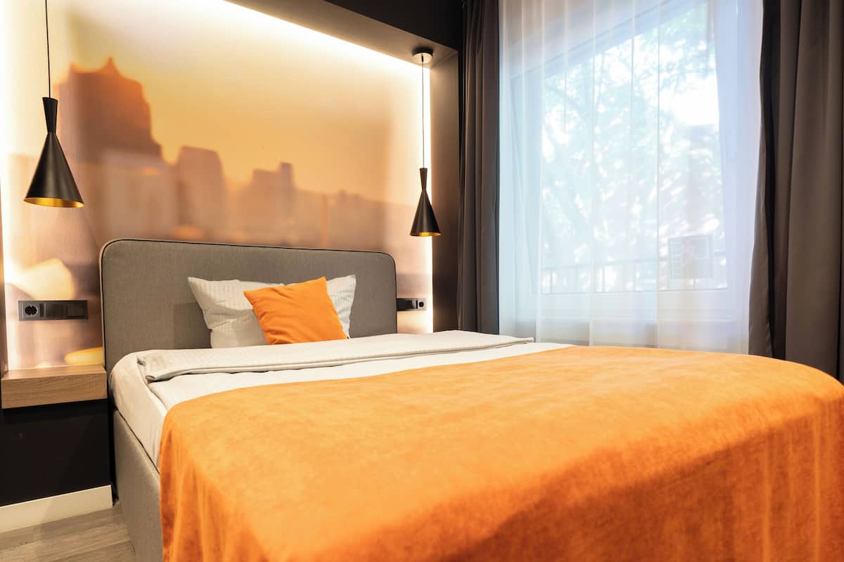 Quarto de hotel moderno com cama bem arrumada, painel decorativo com vista urbana e uma janela grande com cortinas.