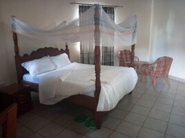 Uma cama de dossel com cortina, uma cadeira de madeira e uma pequena mesa em um quarto com piso de azulejos.