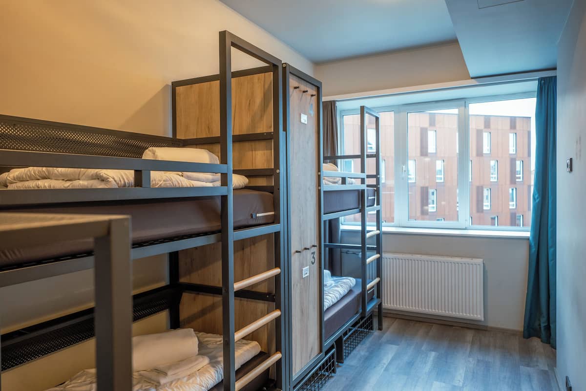 Um quarto de dormitório com beliches, janela com vista para edifícios e um radiador.