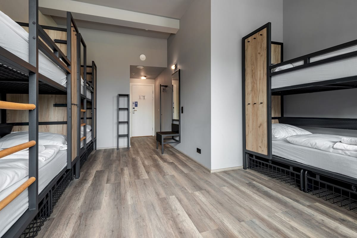 Quarto tipo dormitório com beliches, soalho de madeira e corredor que leva a uma porta.