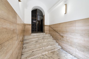 Uma escadaria de mármore com um portão preto no topo, conduzindo a uma porta.