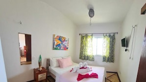 Quarto com cama, mesa de cabeceira, espelho, pintura e janela com cortinas.