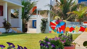 Um pátio com vasos de flores roxas, um edifício branco e um mural na parede.