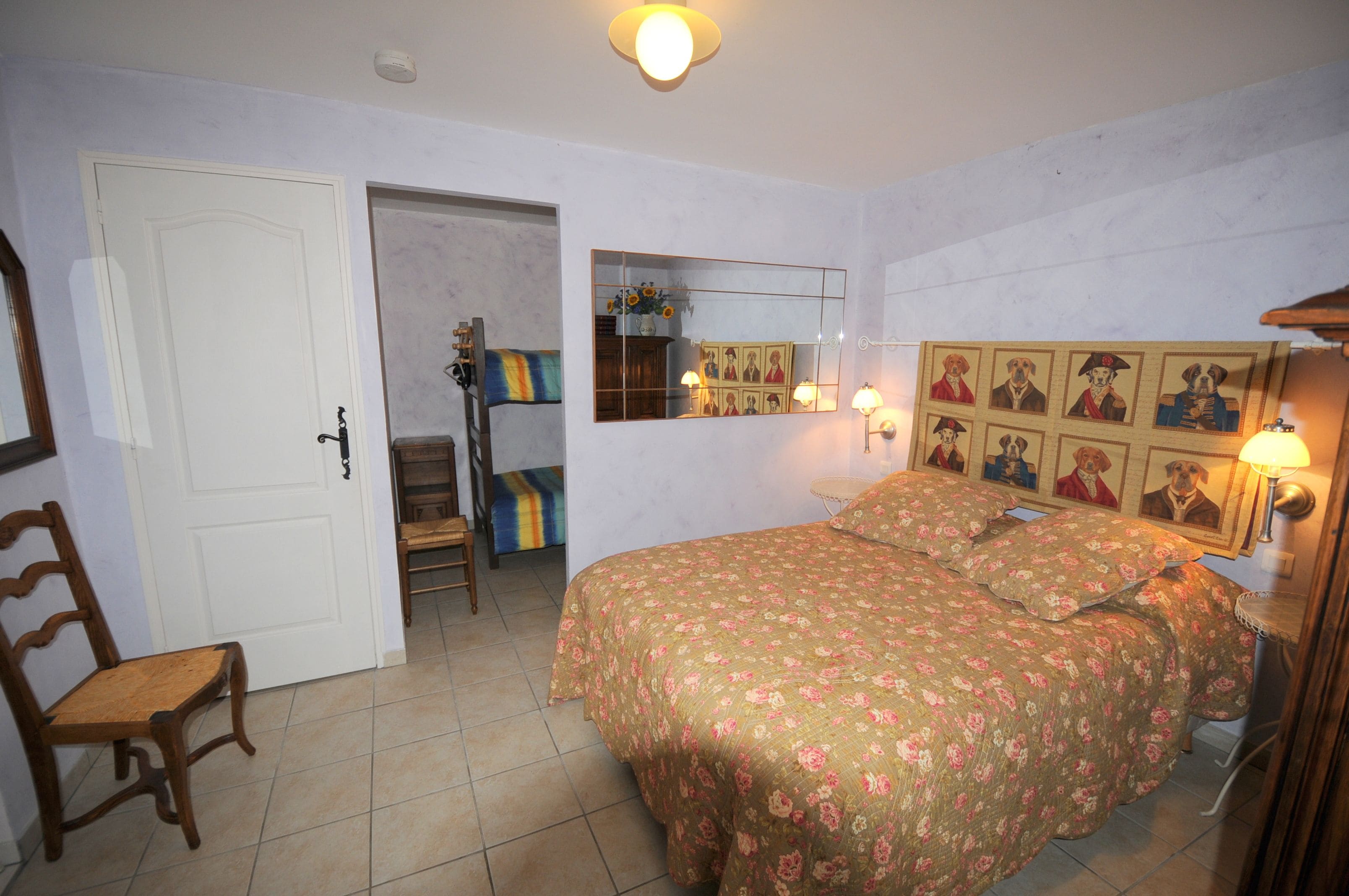 Quarto com cama, cadeira, porta, espelho e luminárias fixadas na parede.
