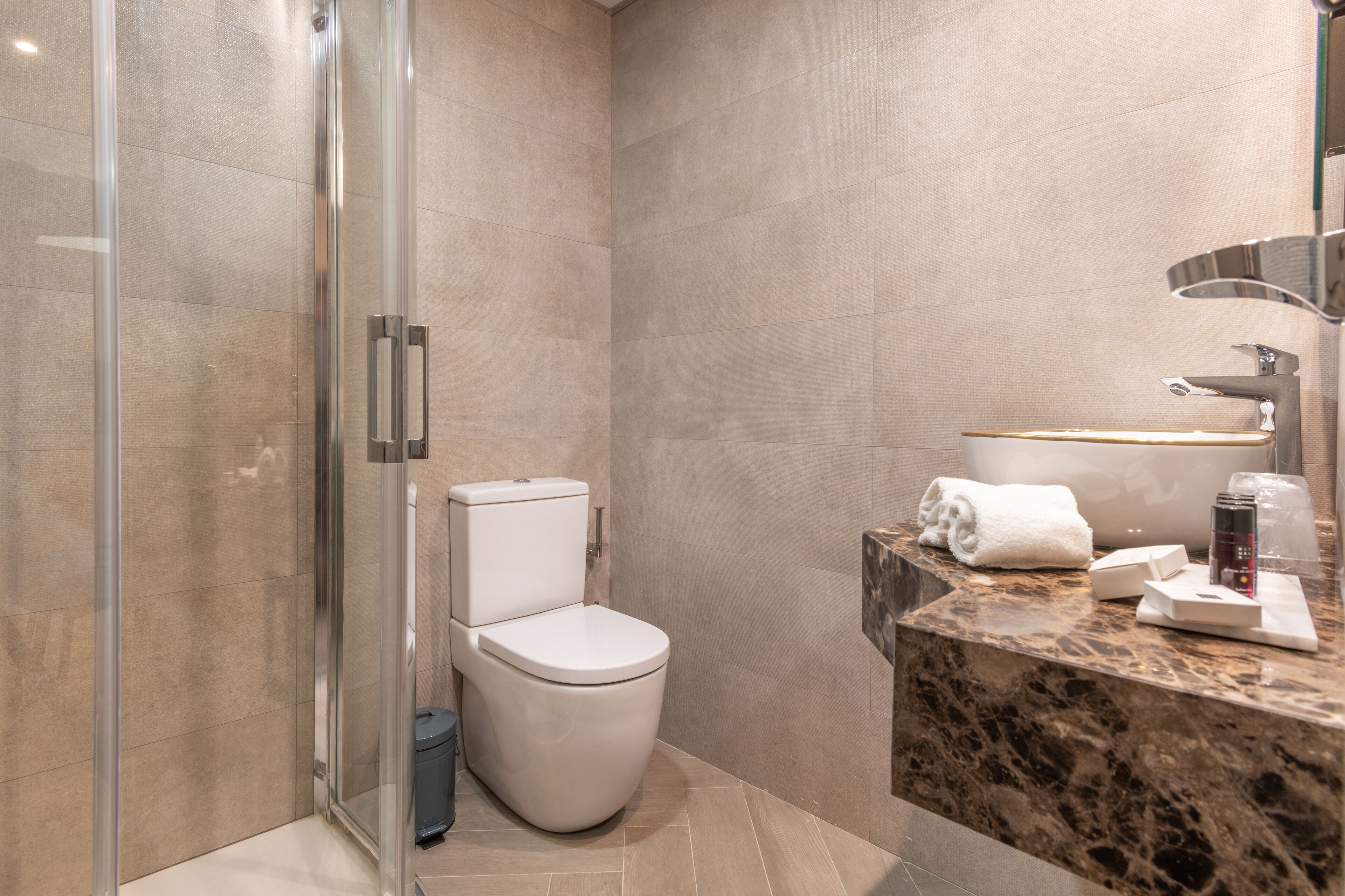 Um banheiro moderno com box de vidro, vaso sanitário, bancada de mármore e porta-toalhas.
