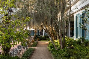 Uma passagem no jardim leva a um edifício com persianas azuis e uma estátua no centro.