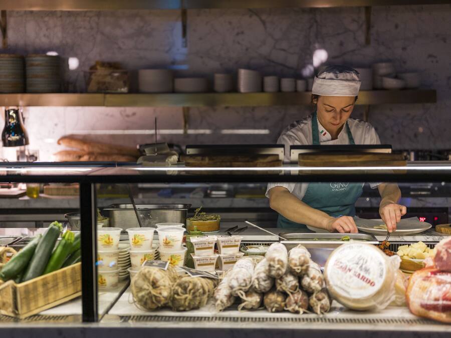Um chef preparando comida em uma cozinha com diversos ingredientes e utensílios à mostra.