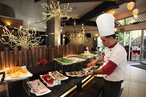 Disposição de buffet com diversos alimentos e um cozinheiro preparando refeições.