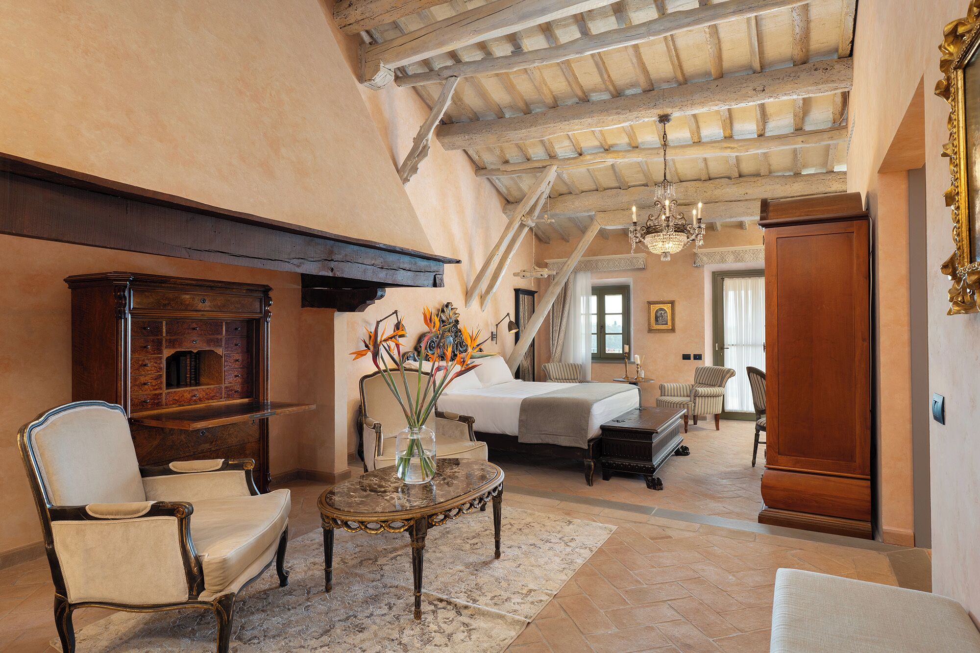 Um quarto amplo com teto alto, lareira, cama, mesa com um vaso de flores e escada que leva a outro andar.