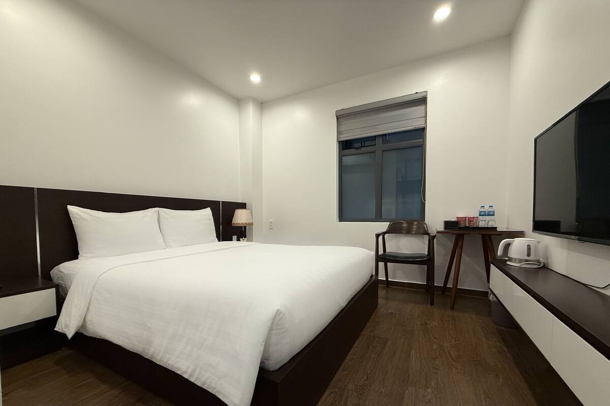 Quarto de hotel com cama, escrivaninha, cadeira, televisão e janela com vista.