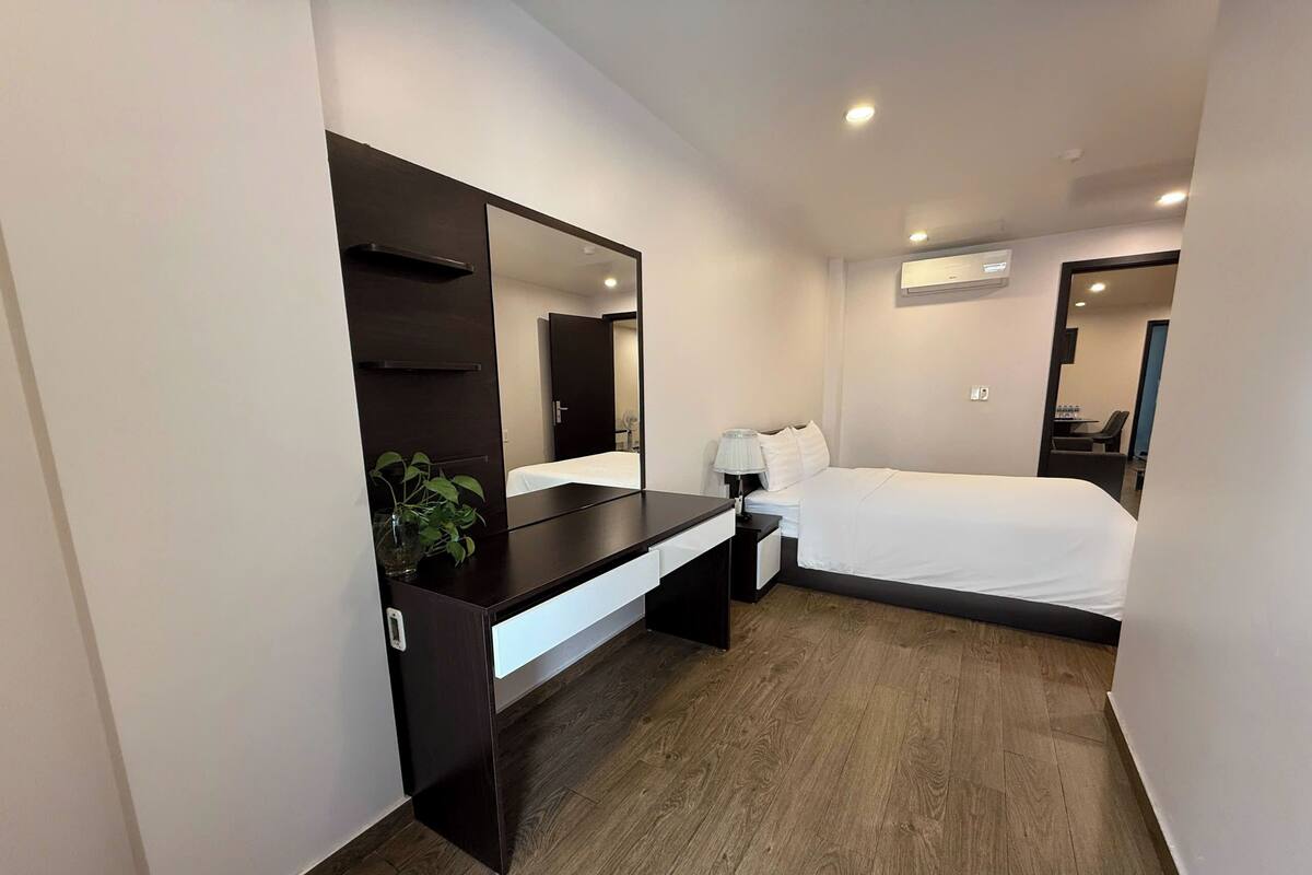 Quarto de hotel moderno com uma cama grande, uma mesa de cabeceira, um espelho e uma pequena planta.