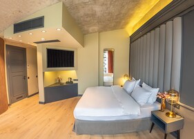 Quarto de hotel moderno com uma cama grande, mesa de cabeceira com luminária, televisão integrada e espelho.