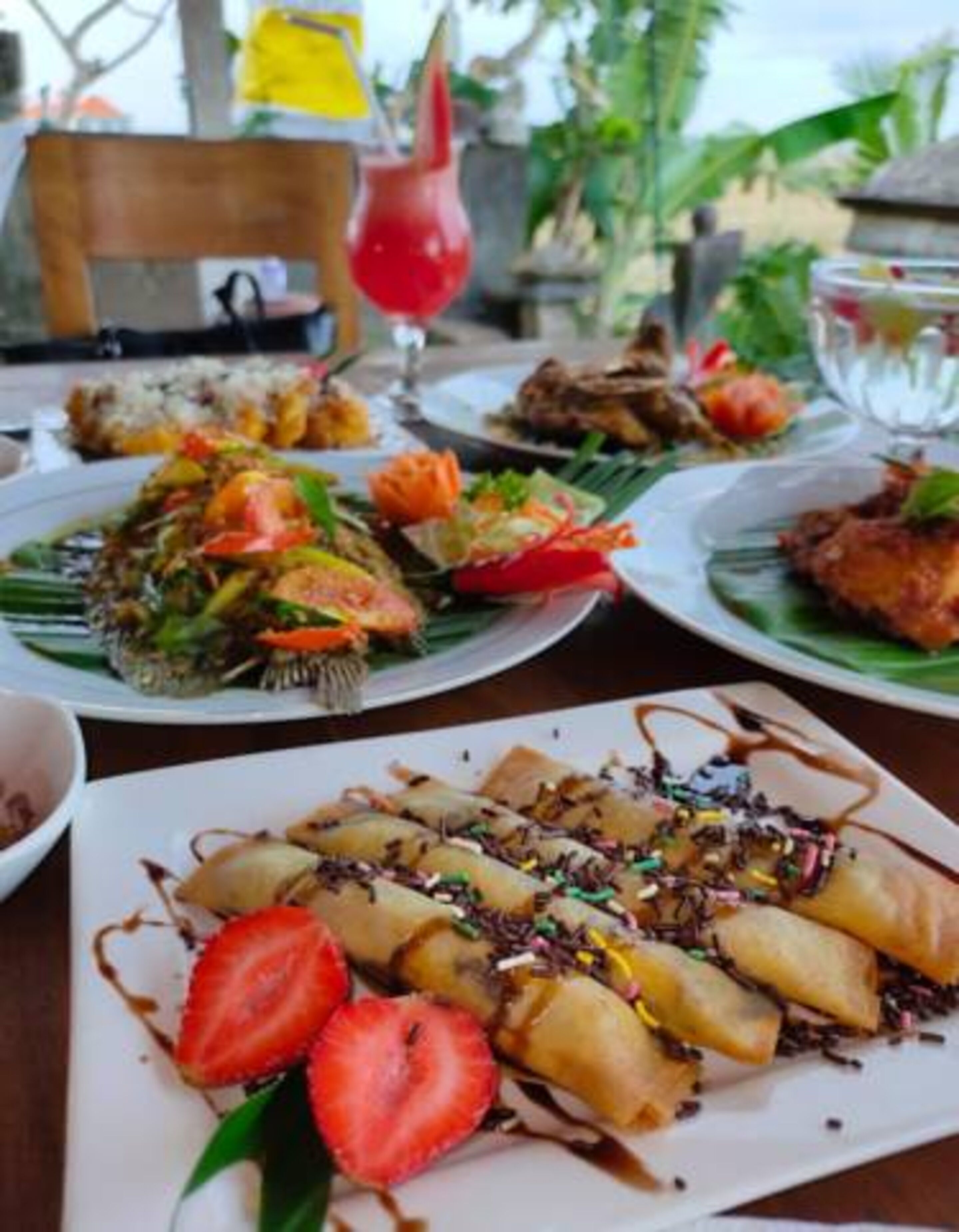 Uma mesa posta com diversos pratos, incluindo uma sobremesa coberta com morangos e um molho, e outro prato com salada e carne grelhada.