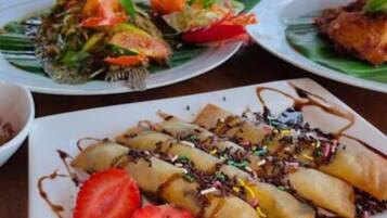 Uma mesa posta com diversos pratos, incluindo uma sobremesa coberta com morangos e um molho, e outro prato com salada e carne grelhada.