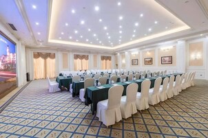 Sala de conferência com uma mesa comprida, cadeiras brancas e um carpete estampado.