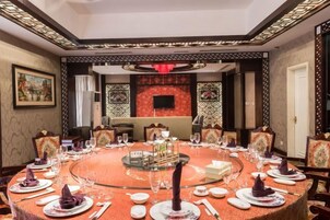 Mesa de jantar redonda com várias cadeiras, uma peça decorativa no centro e uma tela de televisão ao fundo.
