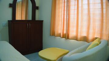 Quarto com uma cama, um banquinho amarelo pequeno, um sofá branco, um guarda-roupa de madeira e uma janela com cortinas laranja.